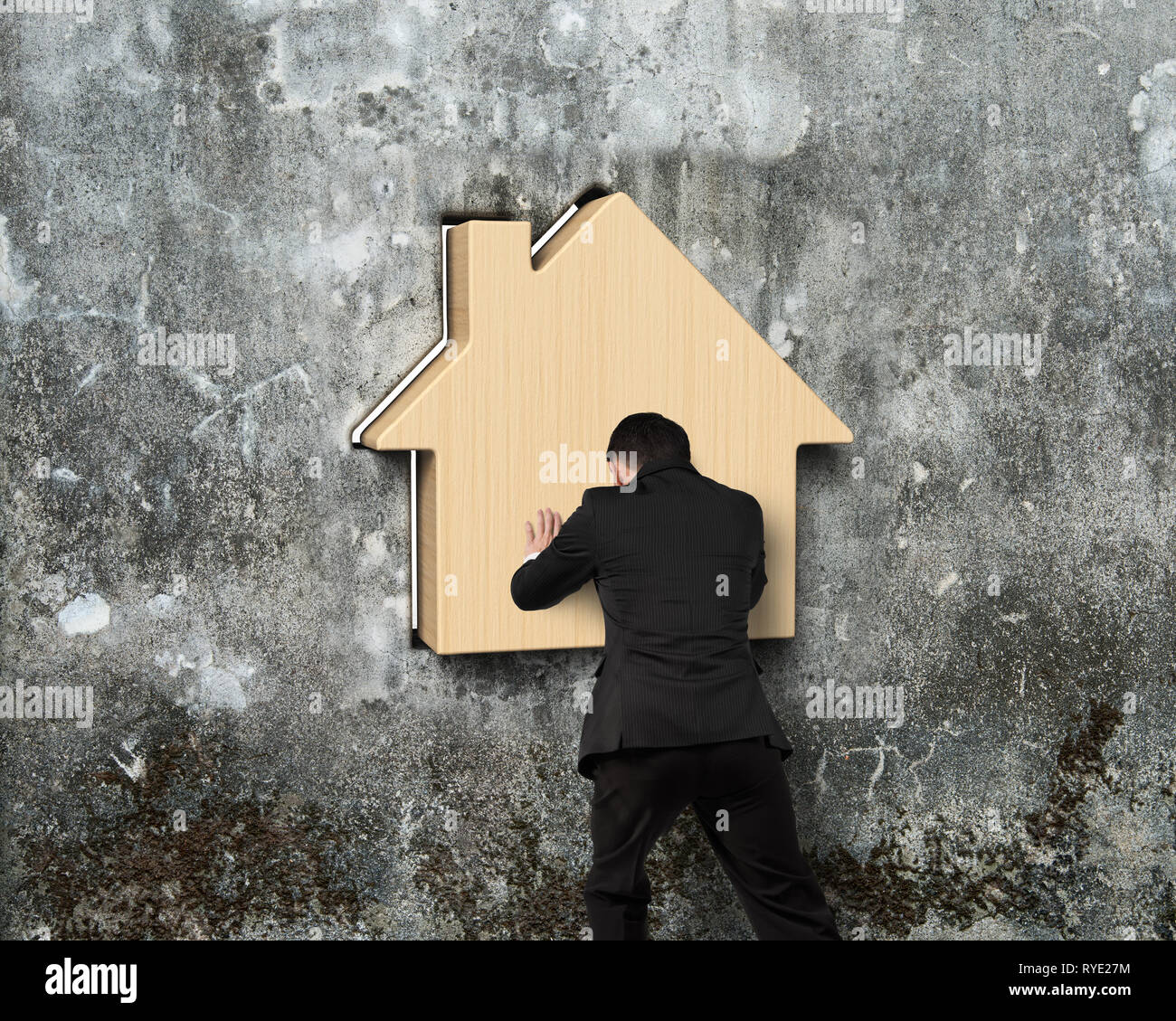 Man pushing wooden house into hole of old mottled concrete wall Stock ...