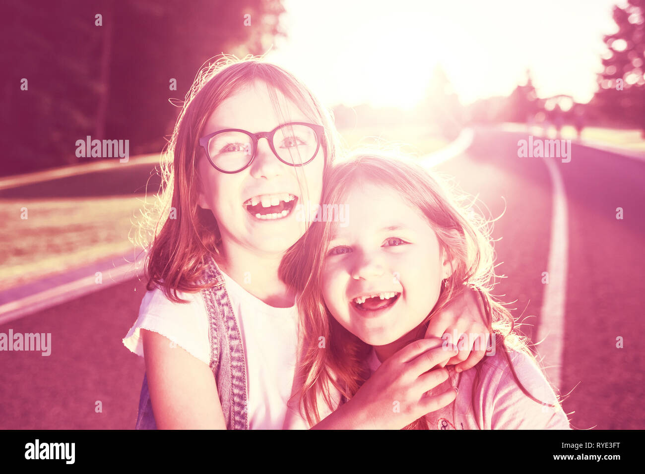 Two joyful girls standing on the road, hugging and smiling against the ...