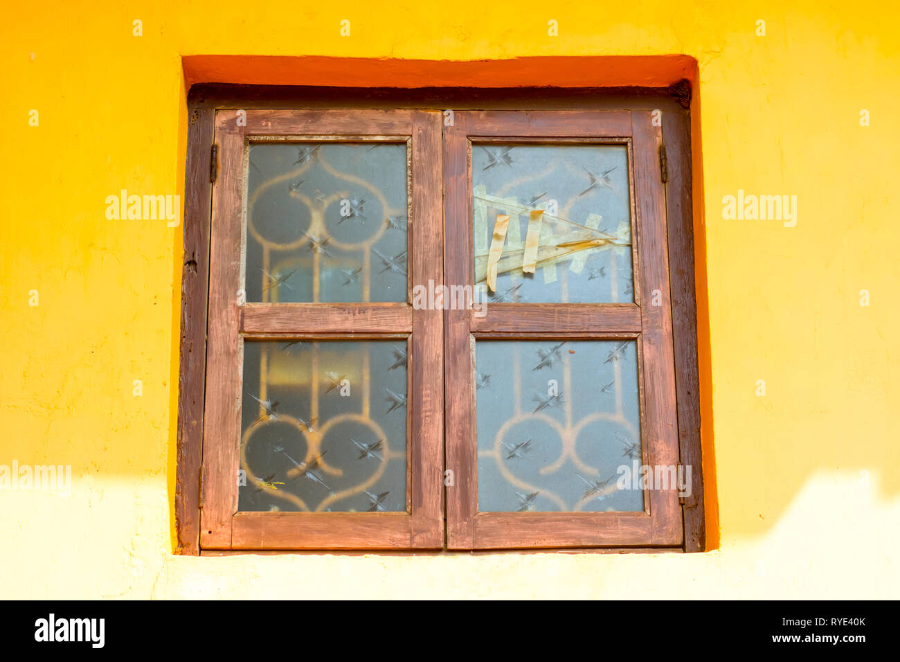 An old broken window is taped up against a yellow wall Stock Photo - Alamy