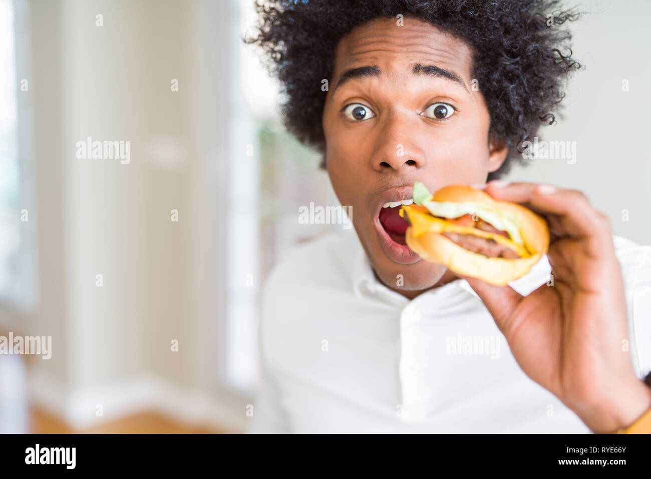 African American hungry man eating hamburger for lunch scared in shock ...