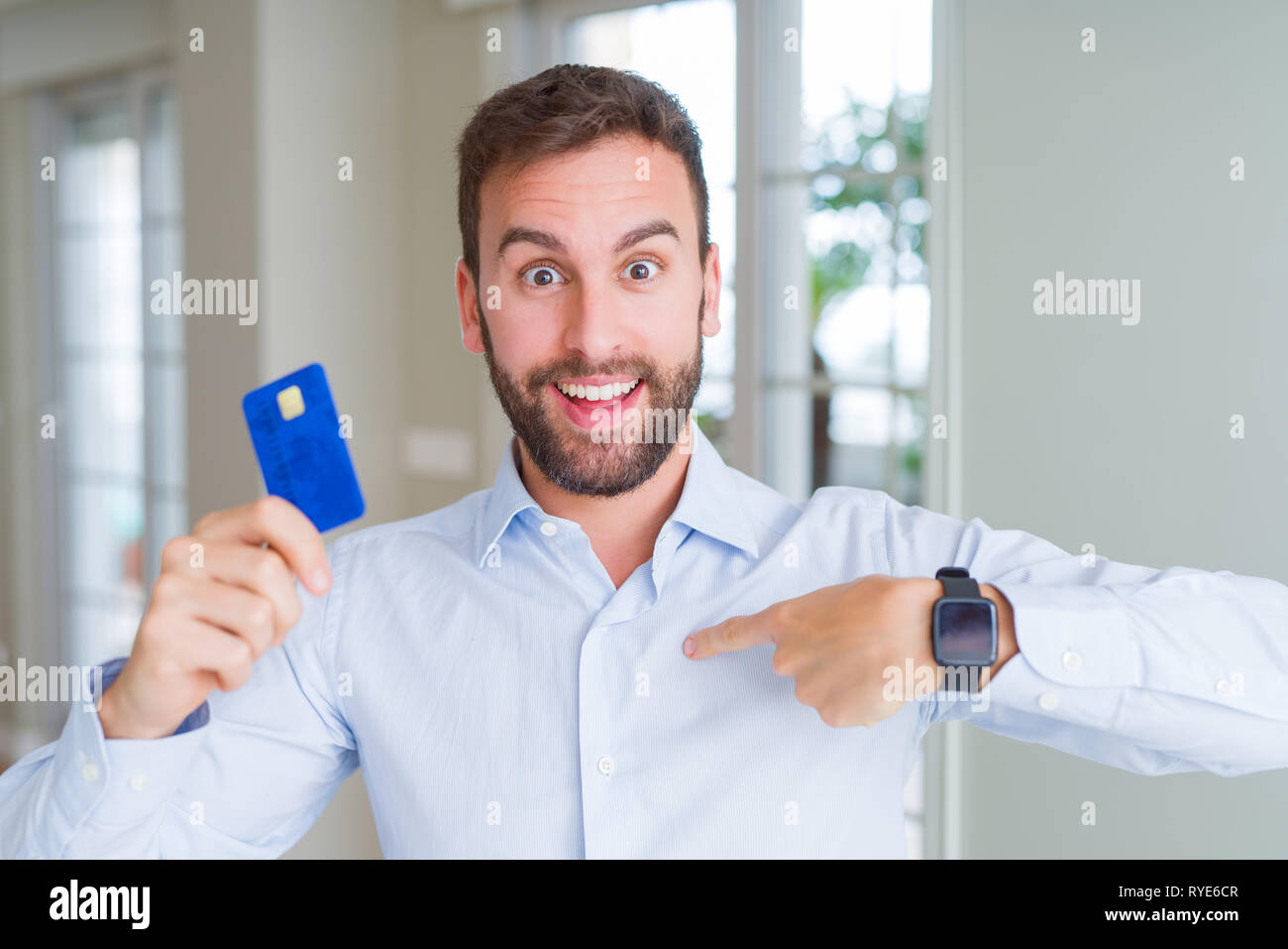Handsome business man holding credit card with surprise face pointing ...
