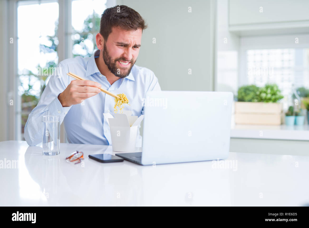 Business man eating take away asian noodles food while working using ...
