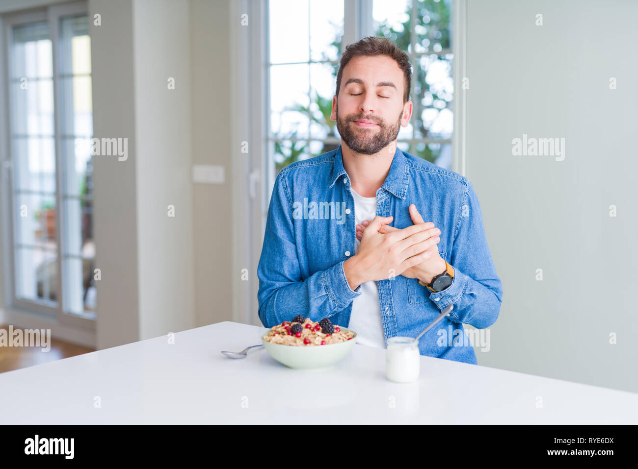 Handsome man eating cereals for breakfast at home smiling with hands on ...