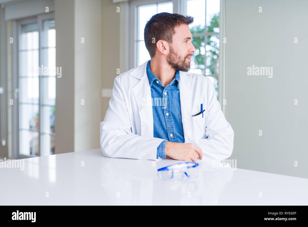 Handsome scientist man wearing white robe and safety glasses looking to ...
