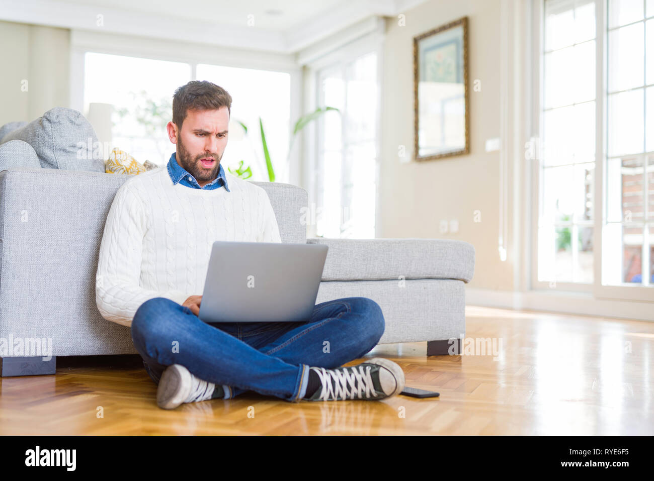 Handsome man wearing working using computer laptop scared in shock with ...