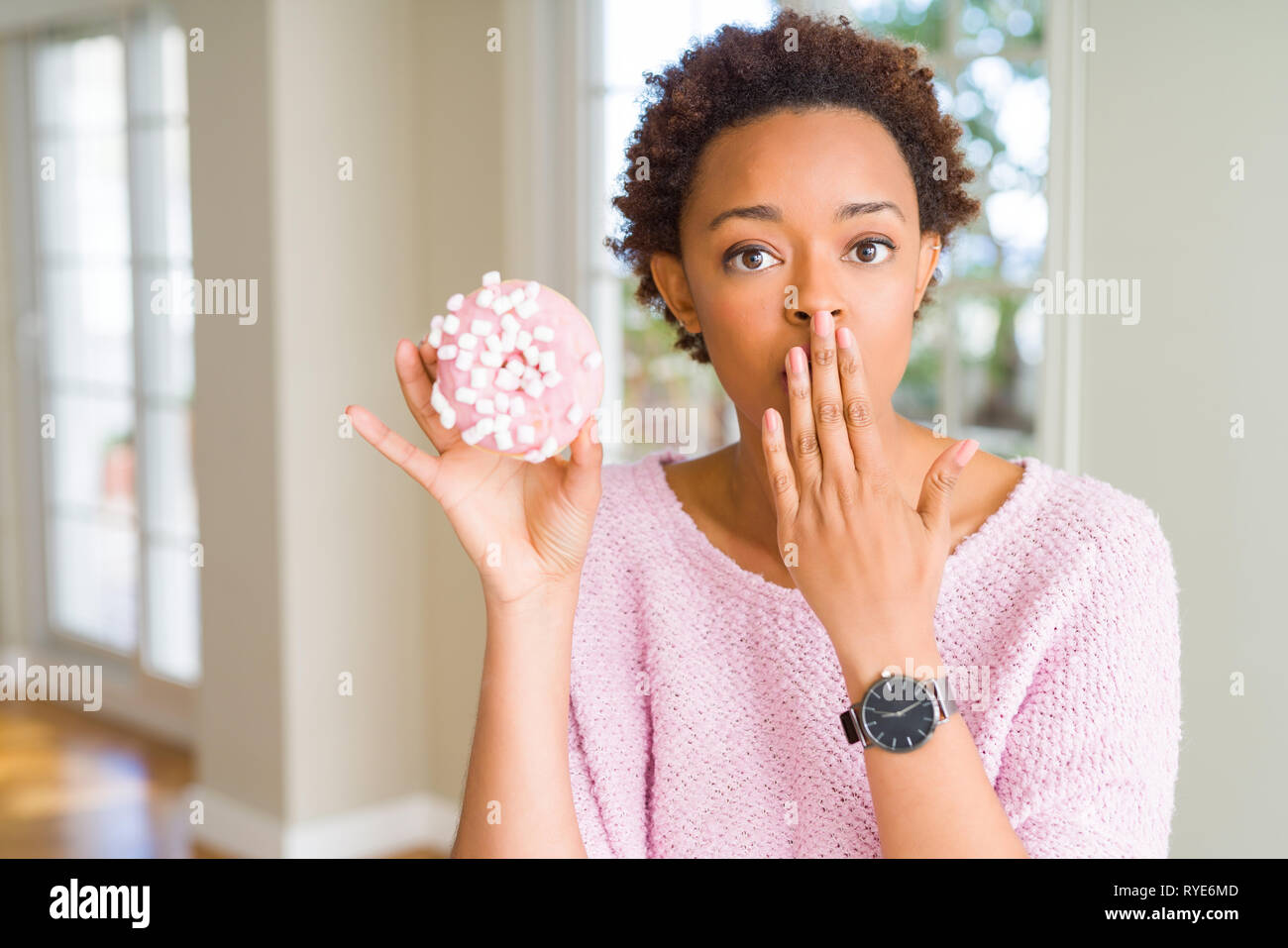 Young african american woman eating pink sugar marshmallows donut cover ...