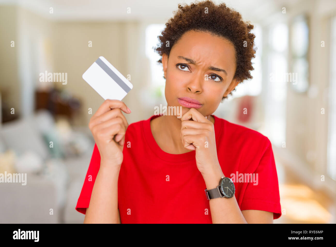 Young african american woman holding credit card serious face thinking ...