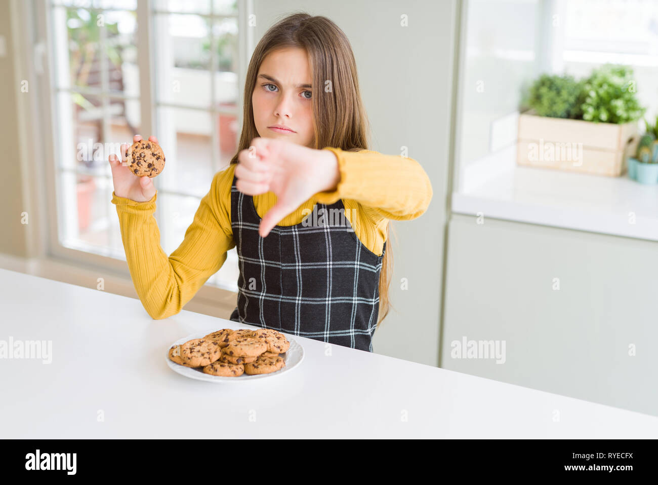 Beautiful young girl kid eating chocolate chips cookies with angry face ...