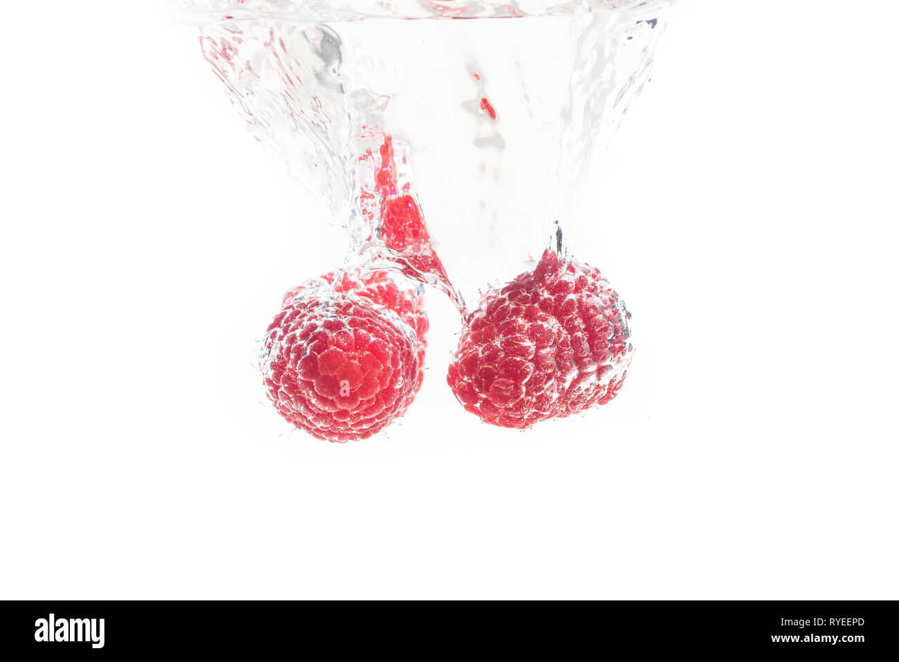 Two juicy, delicious looking raspberries splashing into water surface ...