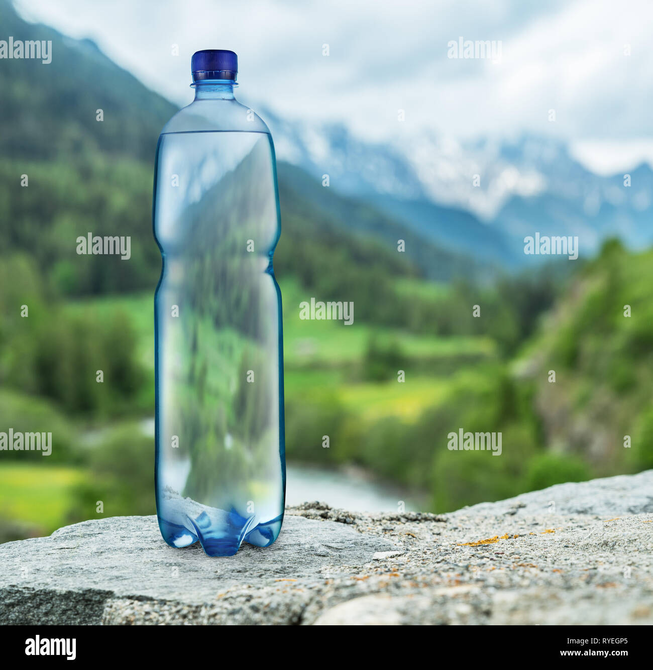 Bottle of water on the stone. Blurred snow mountains tops and green ...
