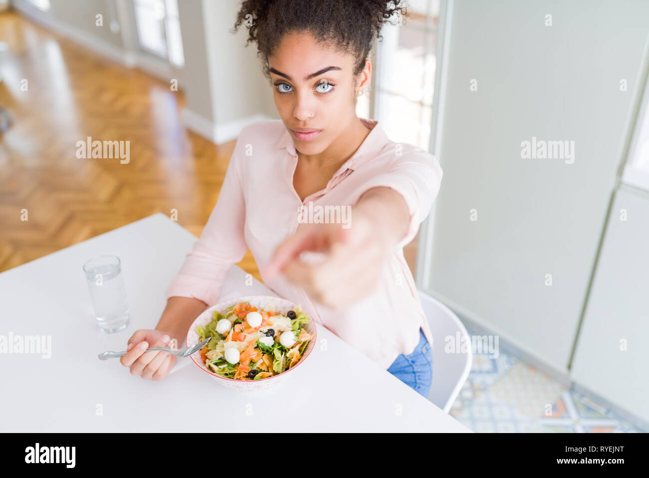 Young african american woman eating healthy pasta salad pointing with ...