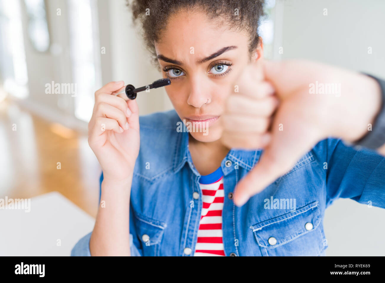 Young african american girl applying eyelashes mascara with angry face ...