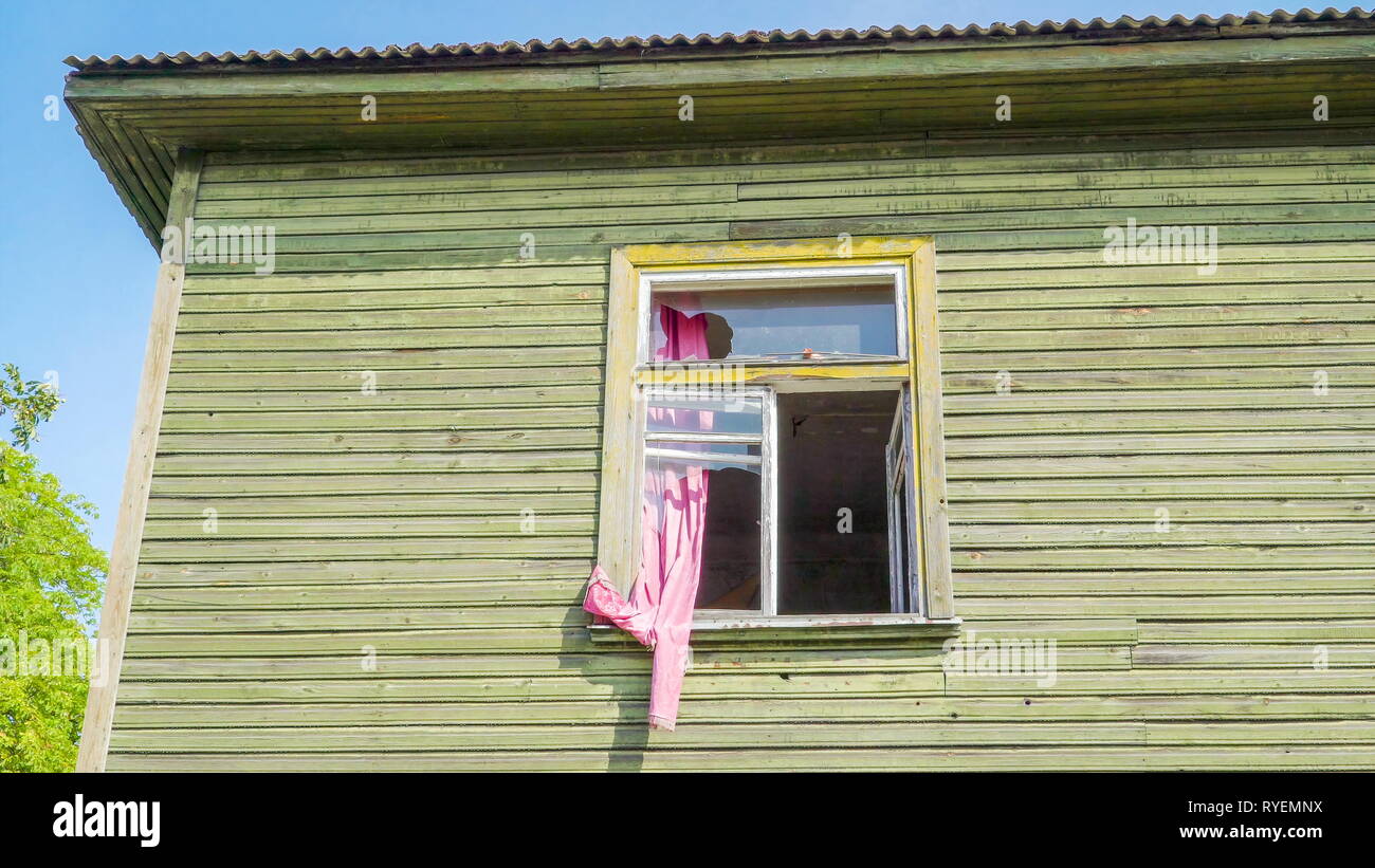 A broken glass of the window of the house with the pink curtain inside ...