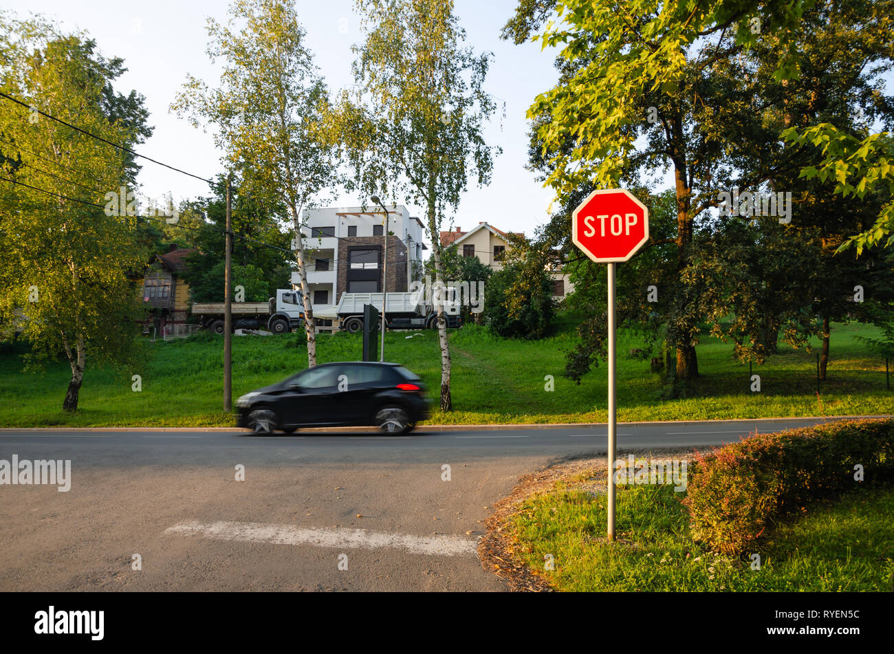Stop sign with a black car in motion on a street behind in the daytime ...