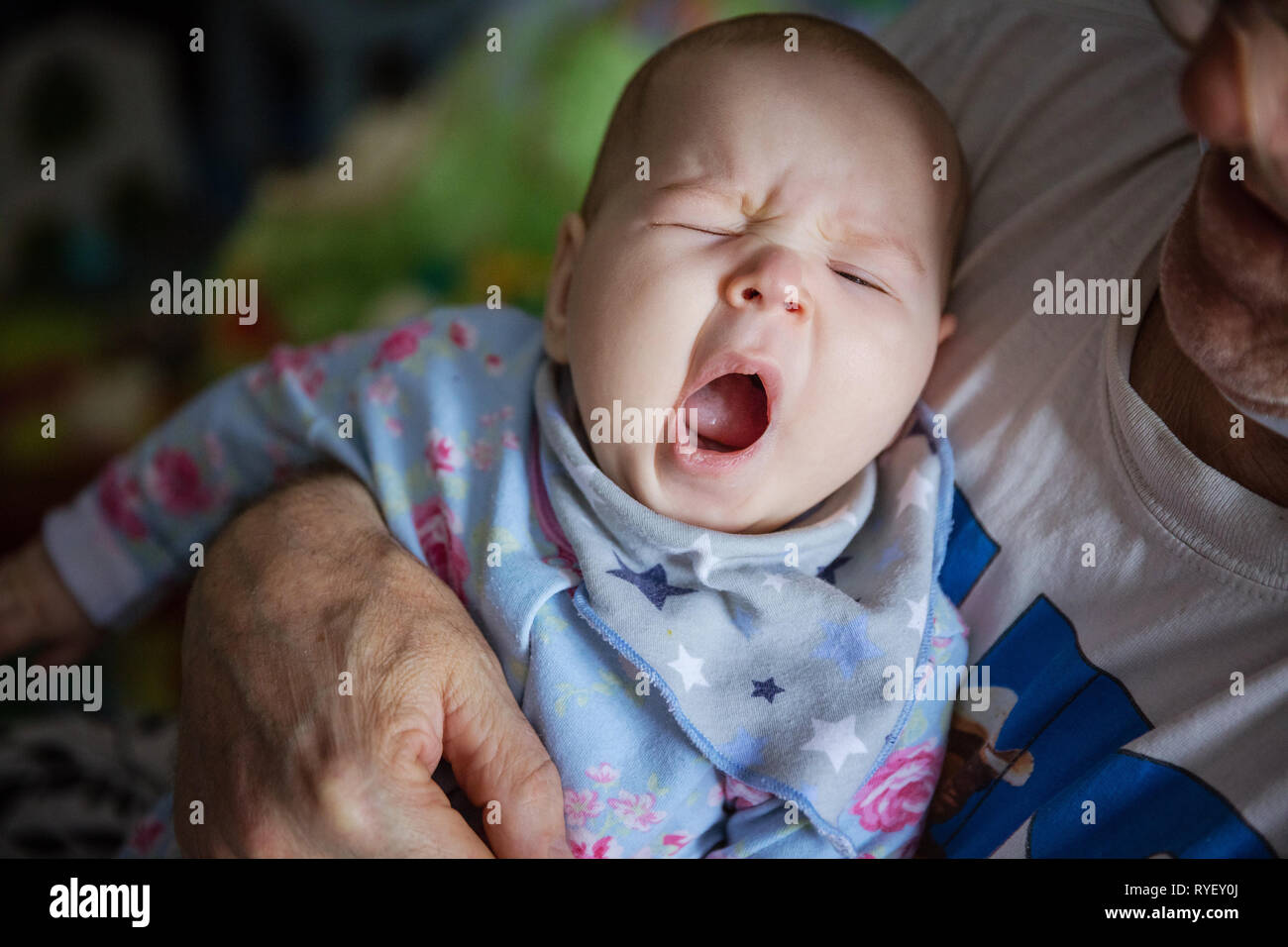 Baby girl yawning. Cropped view of grandfather rocking baby to sleep ...