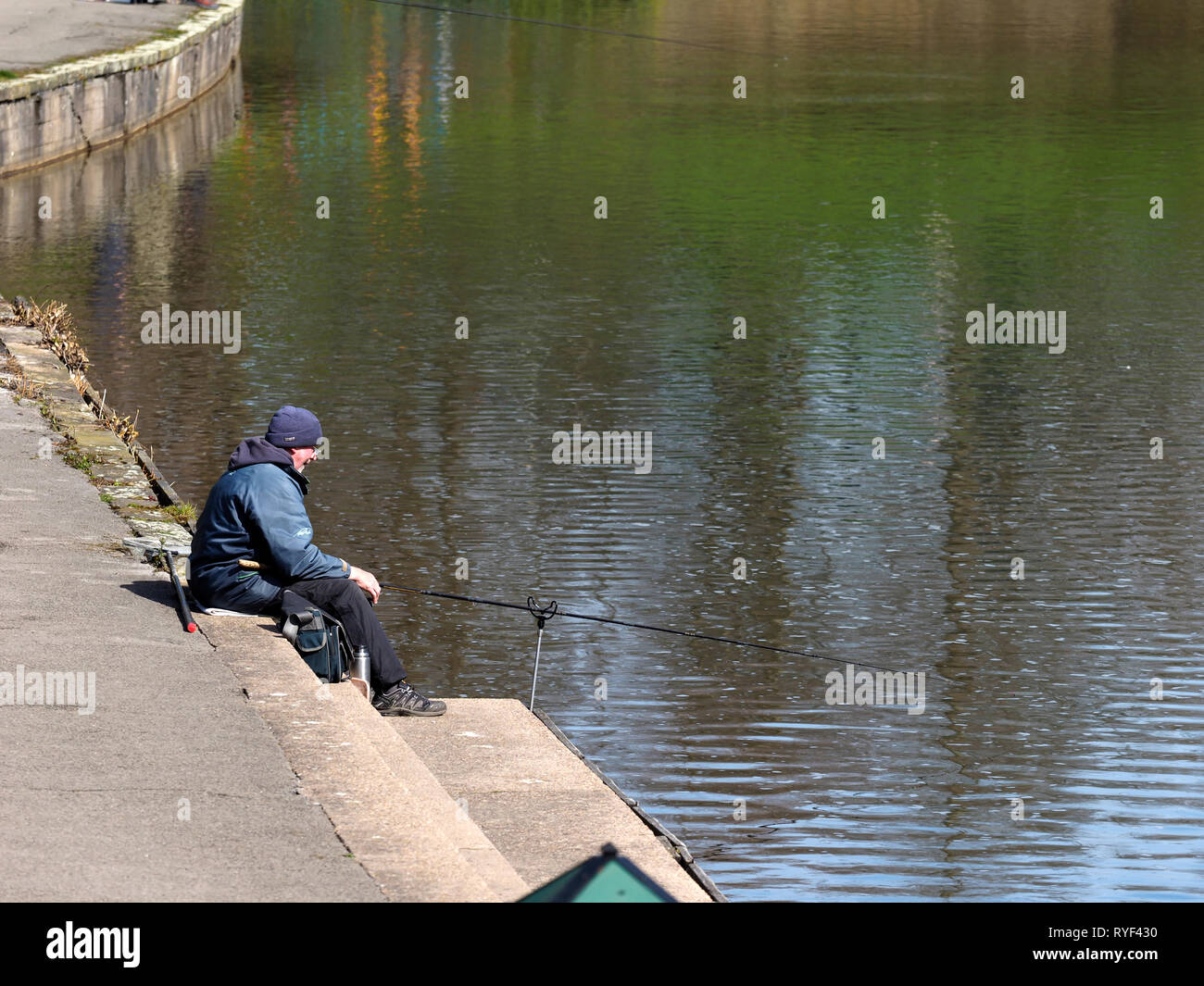 Person sitting at side of lake fishing with rod England Stock Photo - Alamy
