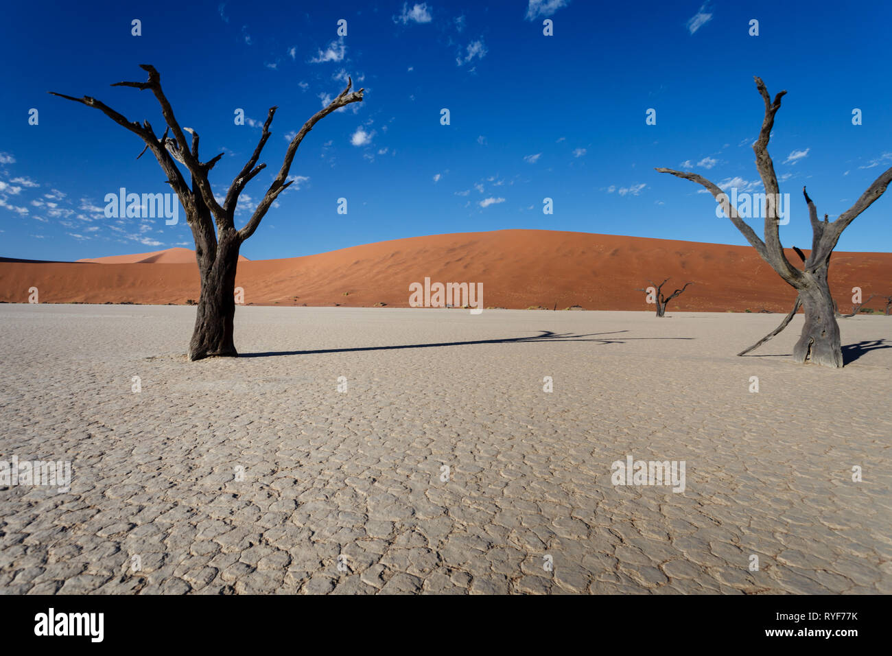 Sun shines on sand mountains behind cracked dried mud in riverbed and a ...