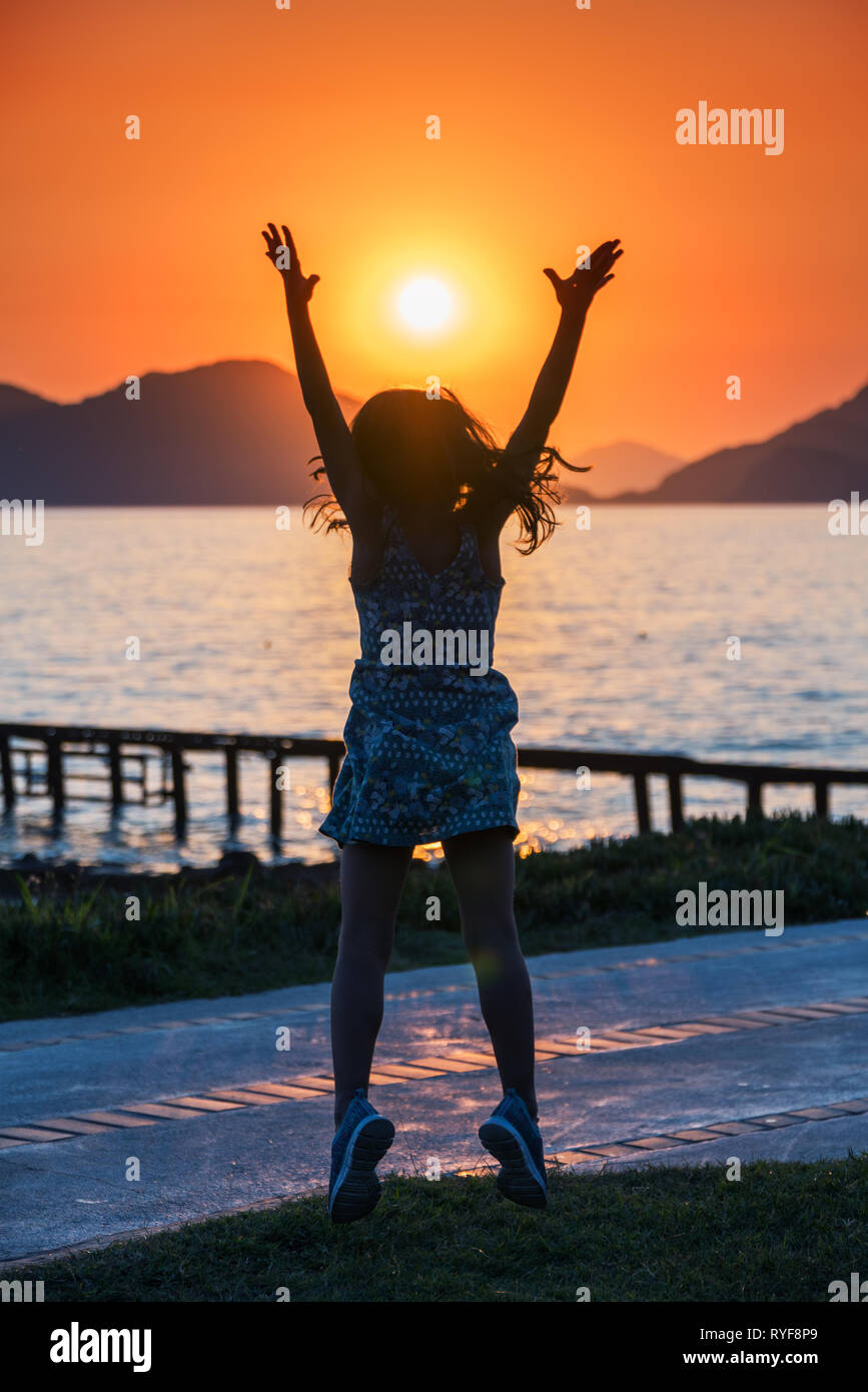 Little girl is enjoying sunset at the sea coast. Girl's silhouette at ...