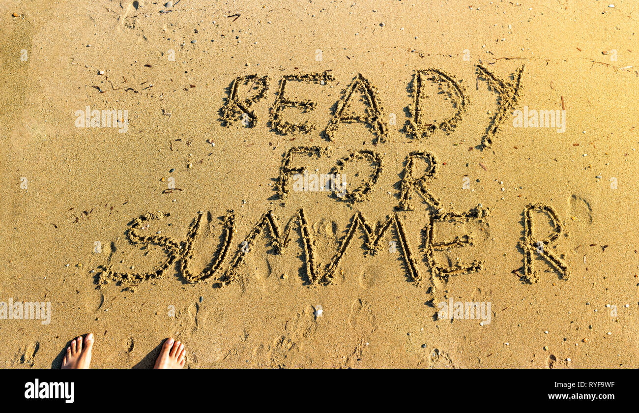 Hand written in sand ready for summer words top view with feet ...