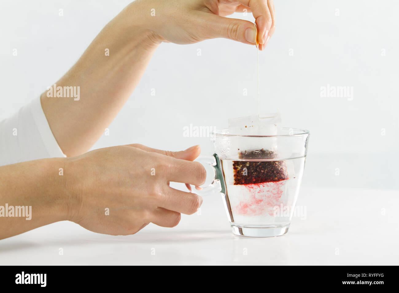 Close-up of a woman hand dipping a sachet of Hibiscus Tea in a glass ...