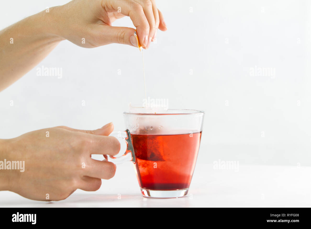 Close-up of a woman hand dipping a sachet of Hibiscus Tea in a glass ...