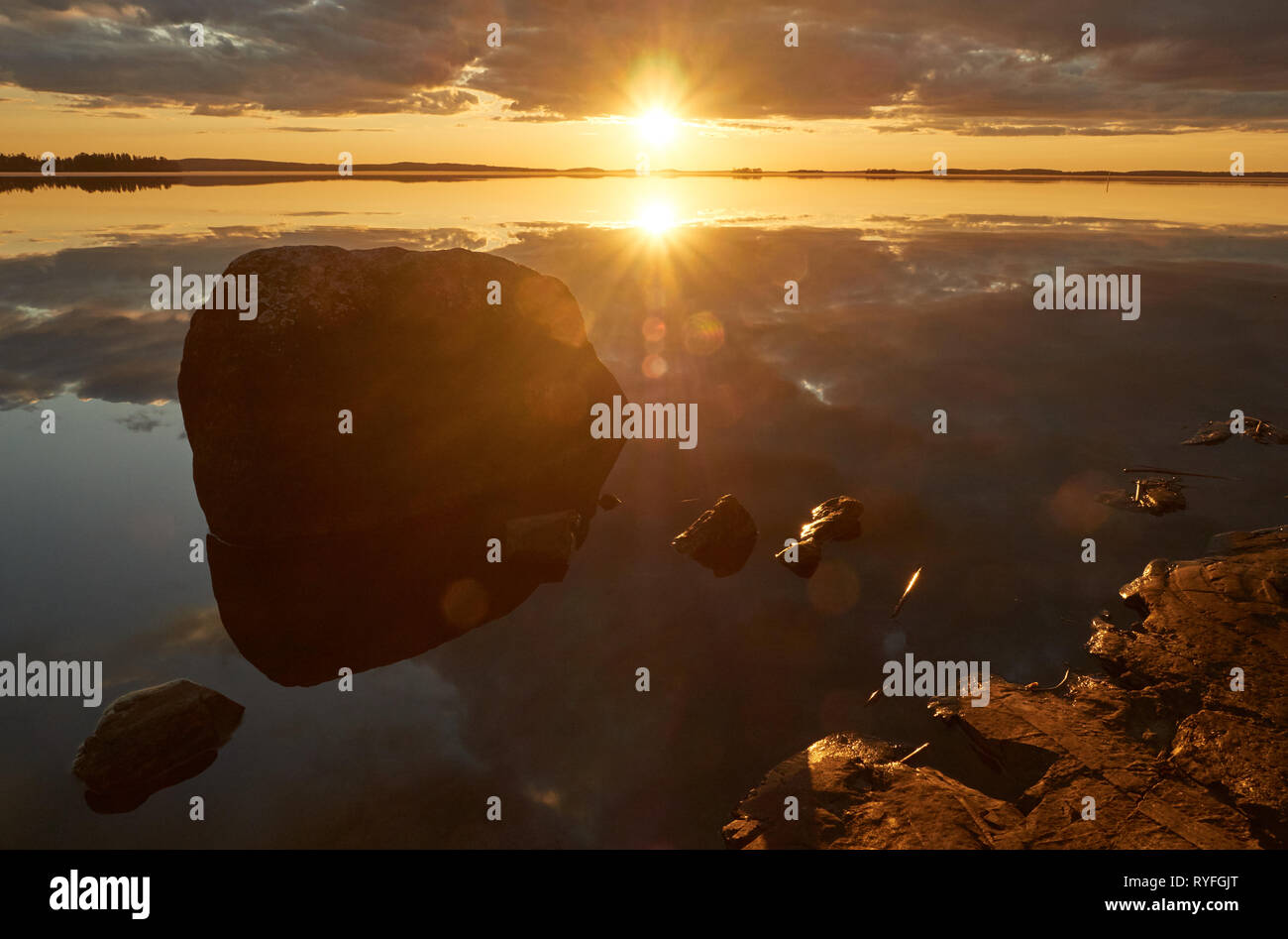 Warm and vibrant golden sunset with red color on the rocks of the shore ...