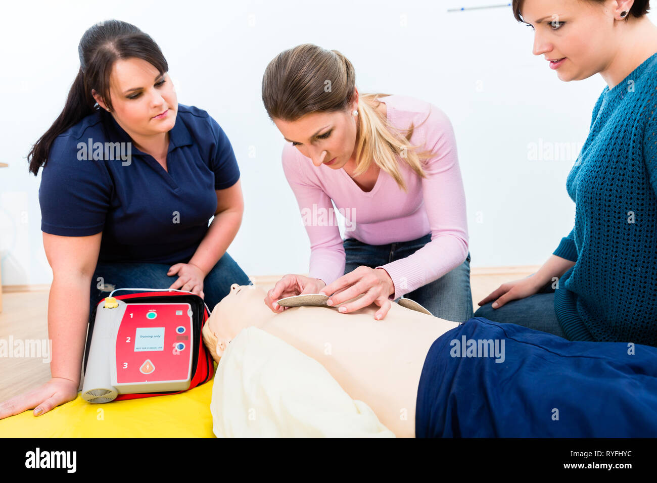 Female attendees of first aid class learning how to use defibrillator ...