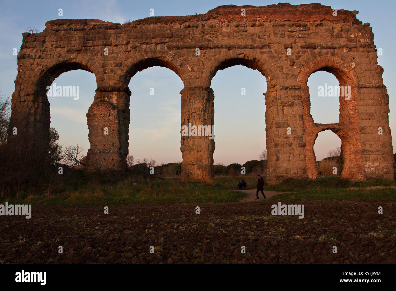 Solitary walker at sunset under the Claudian and Anio Novus Aqueducts ...