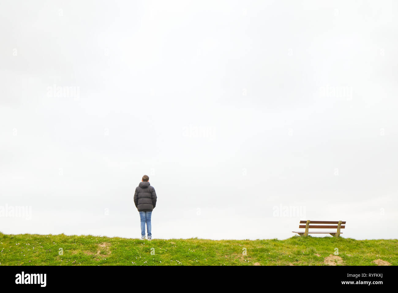 A single person standing next to a single empty wooden bench on the ...