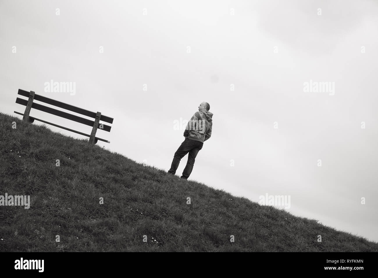 A single person standing next to a single empty wooden bench on the ...