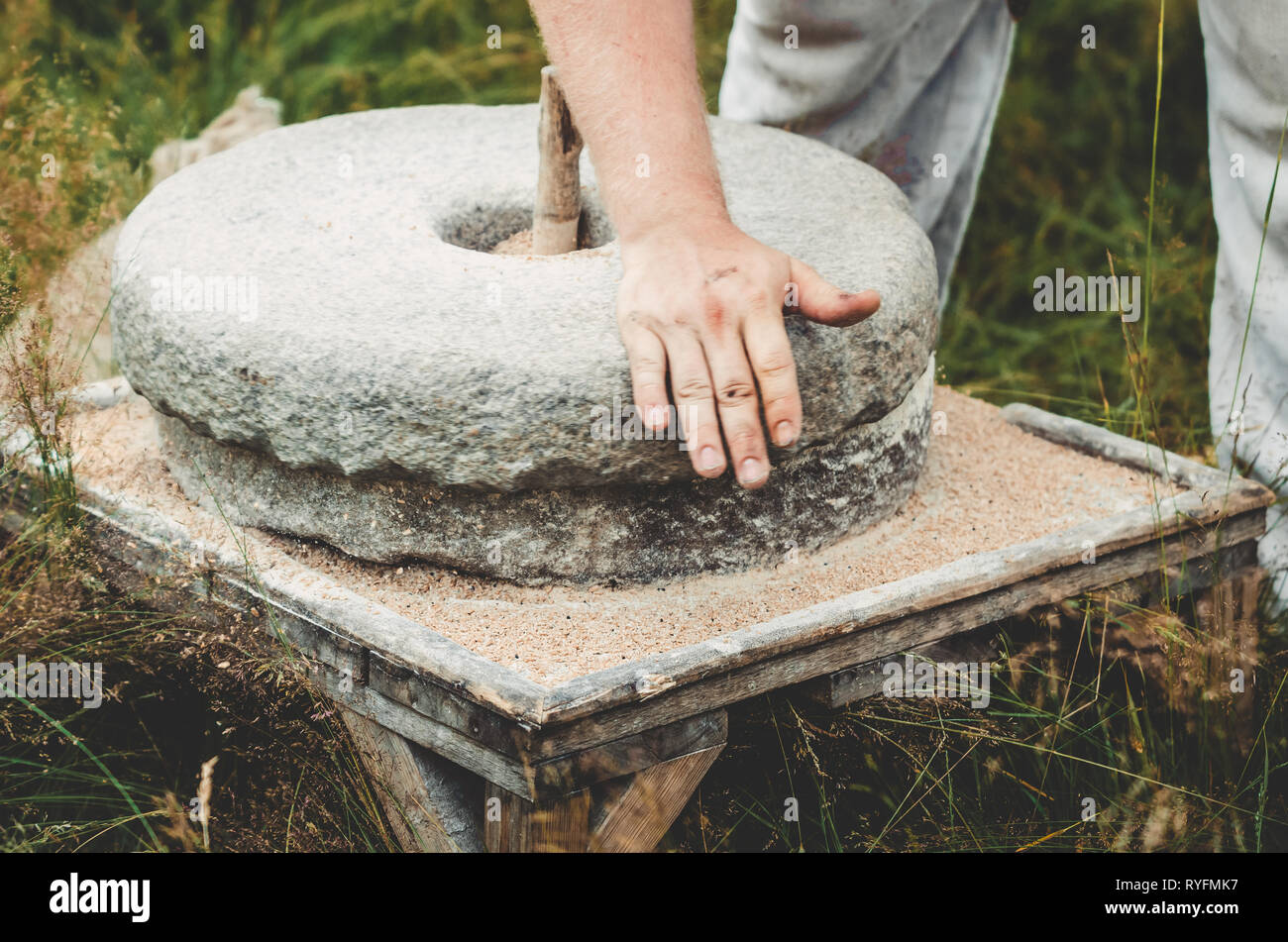 The ancient quern stone hand mill with grain. The man grinds the grain ...