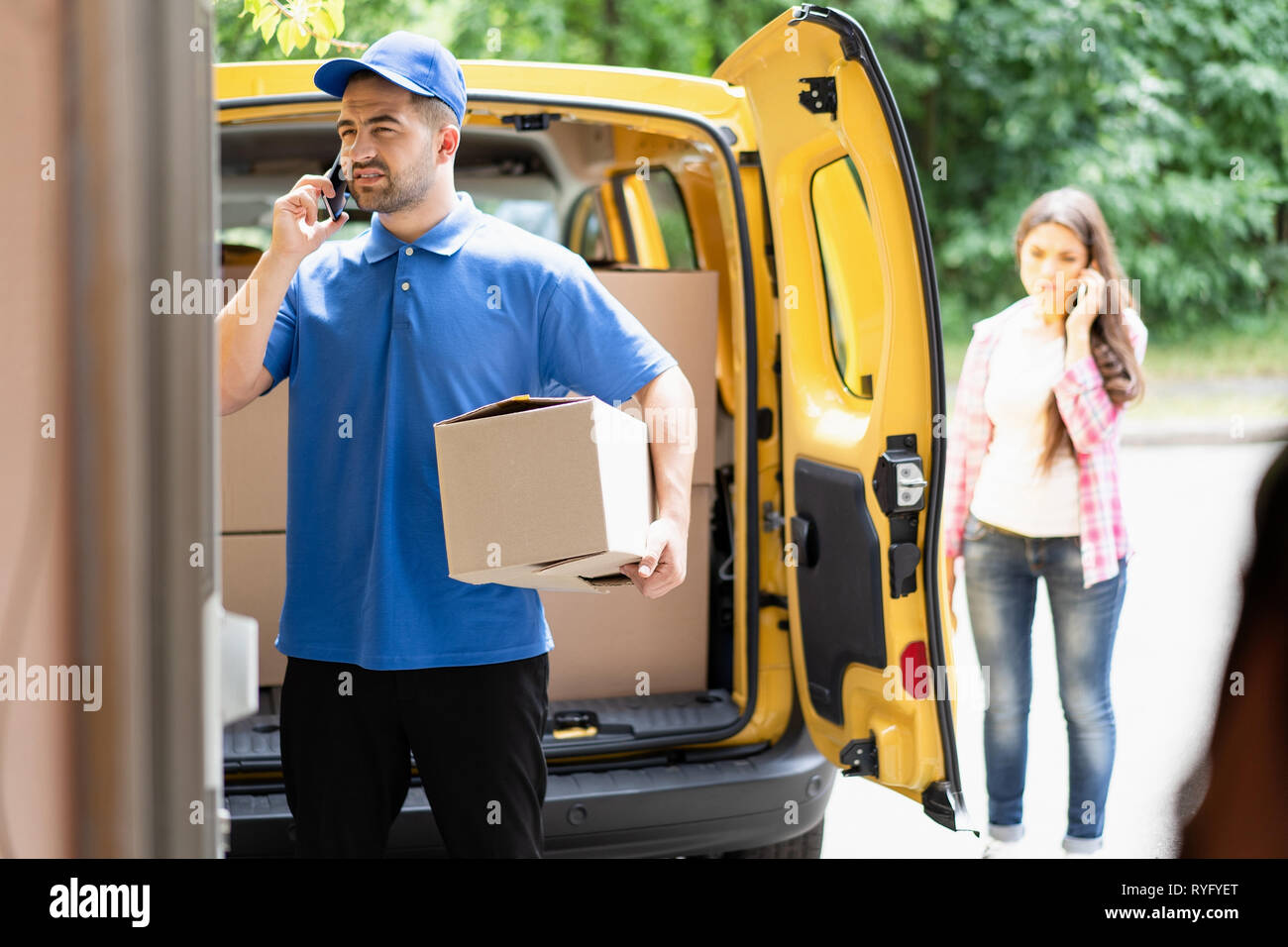Delivery Man Wearing Blue Uniform Holding Cardboard Box And Talking On