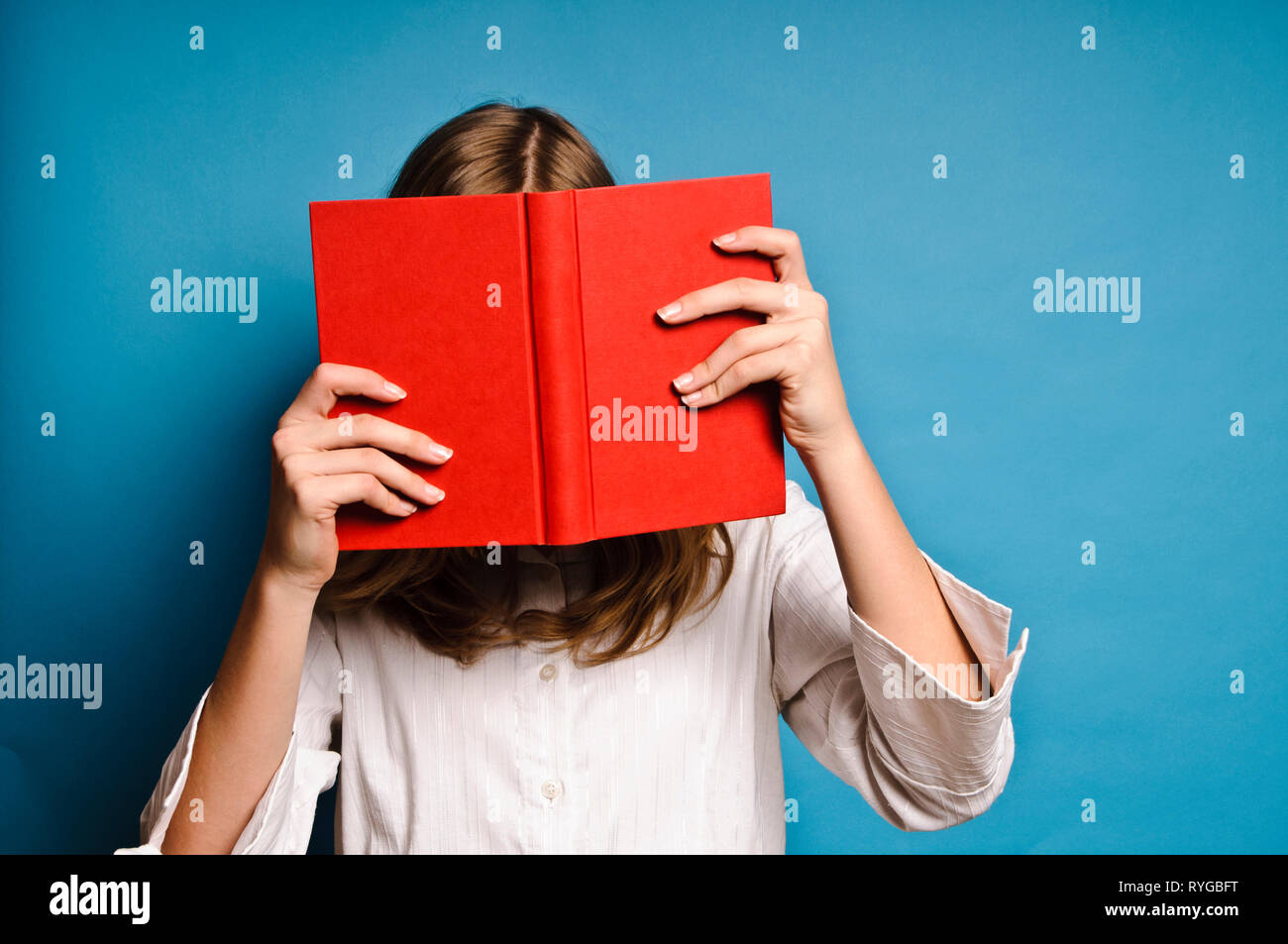 blonde girl hiding behind a red book Stock Photo - Alamy