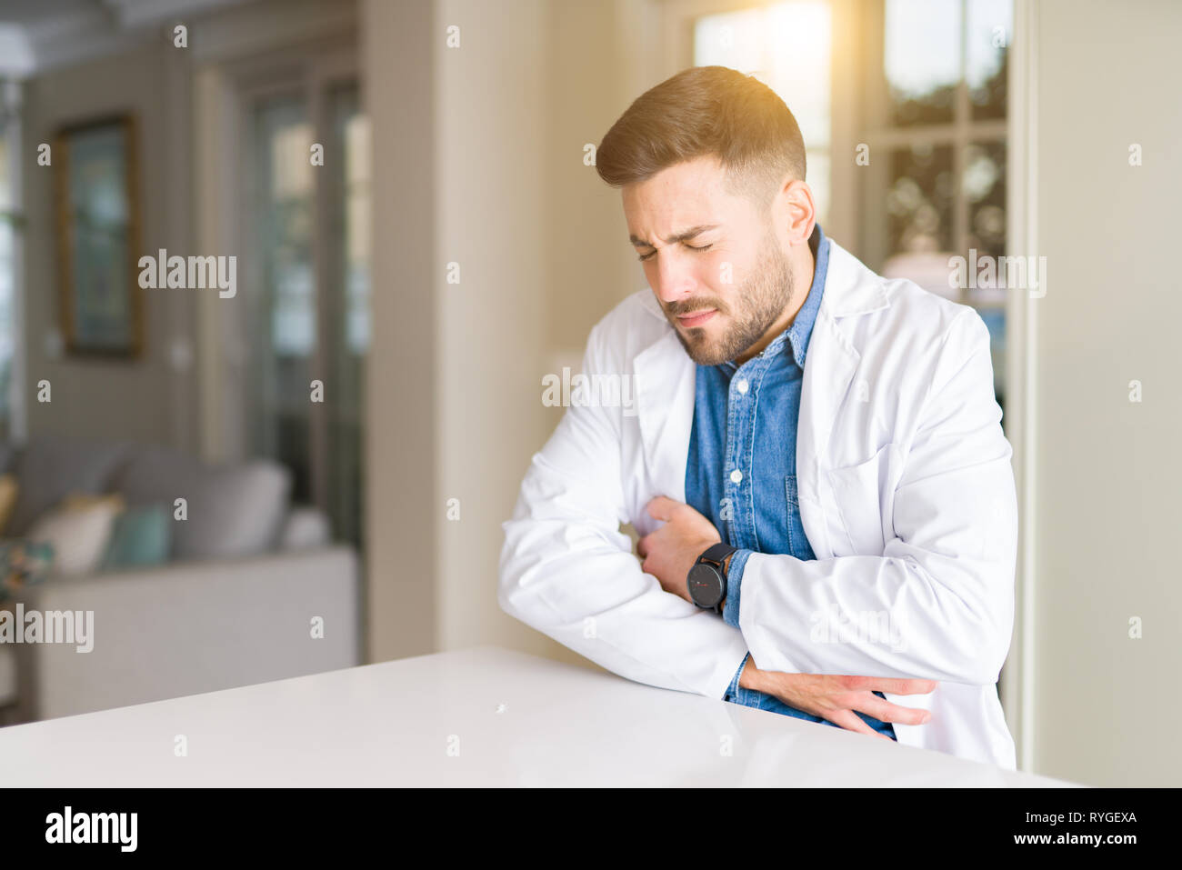 Young handsome doctor man at the clinic with hand on stomach because ...