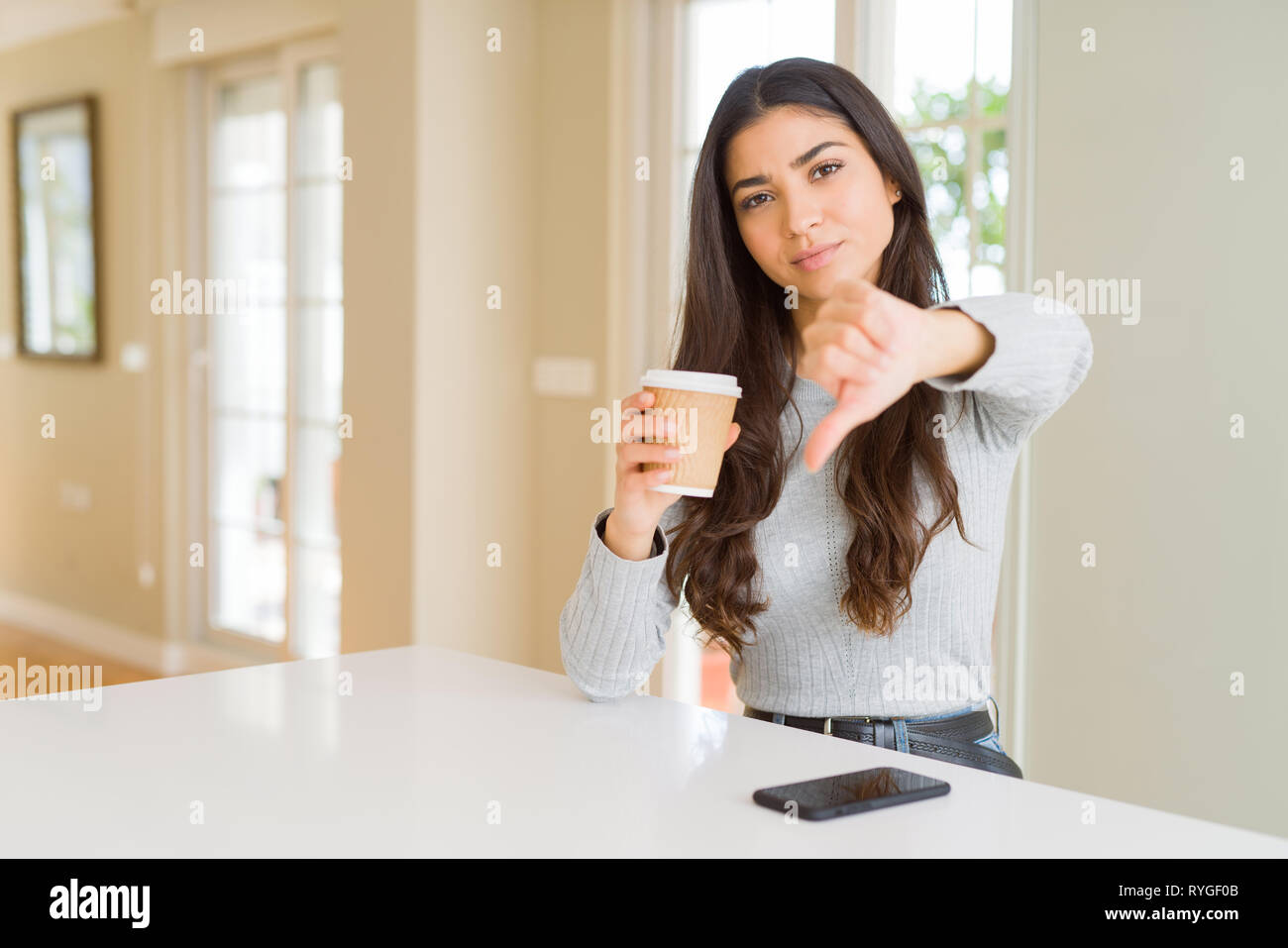 Young woman drinking a cup of coffee at home with angry face, negative ...