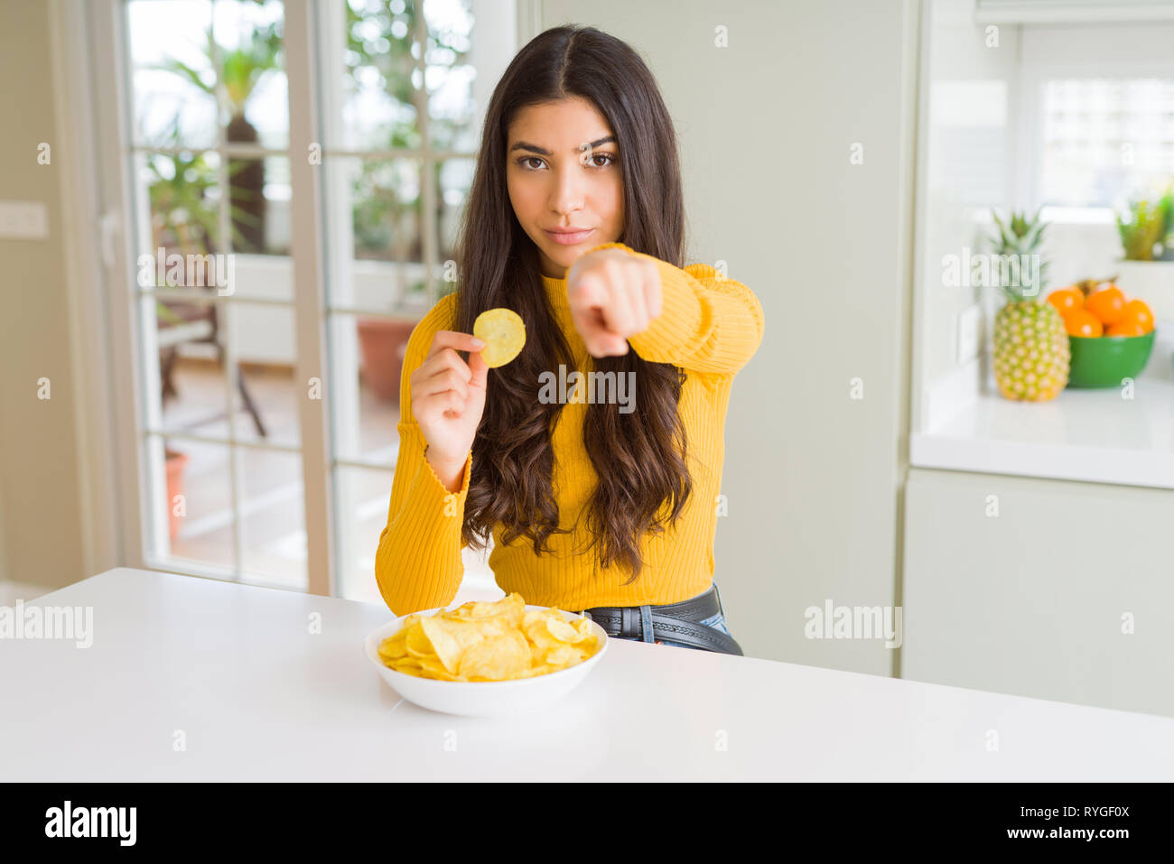 Young woman eating fastfood potato chips pointing with finger to the ...
