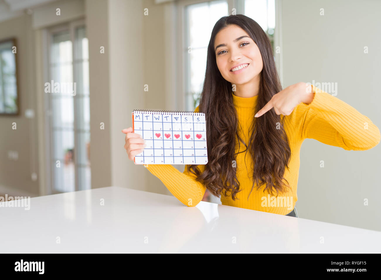 Young woman holding menstruation calendar with surprise face pointing ...