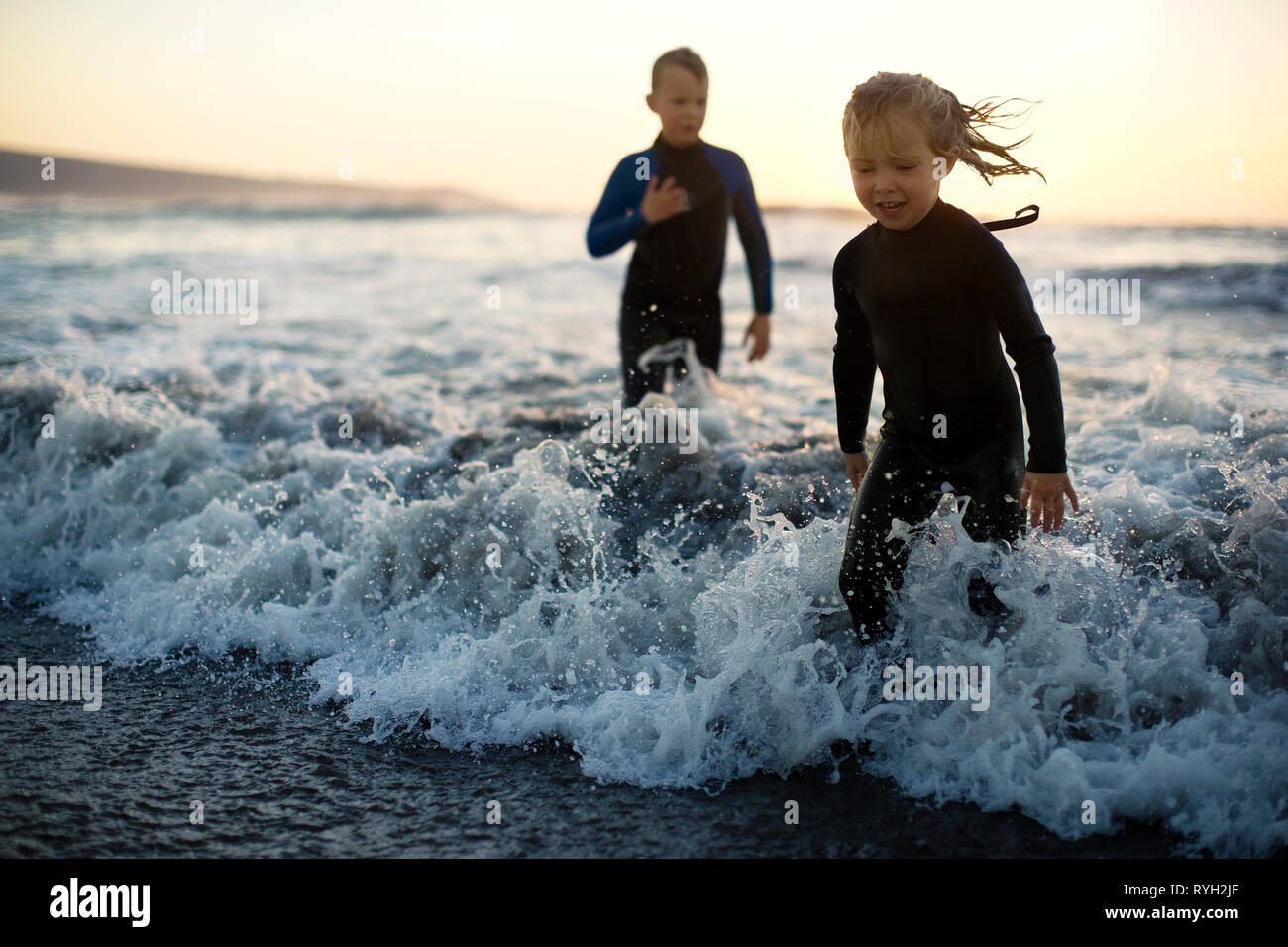Two young children playing in the surf at sunset Stock Photo - Alamy