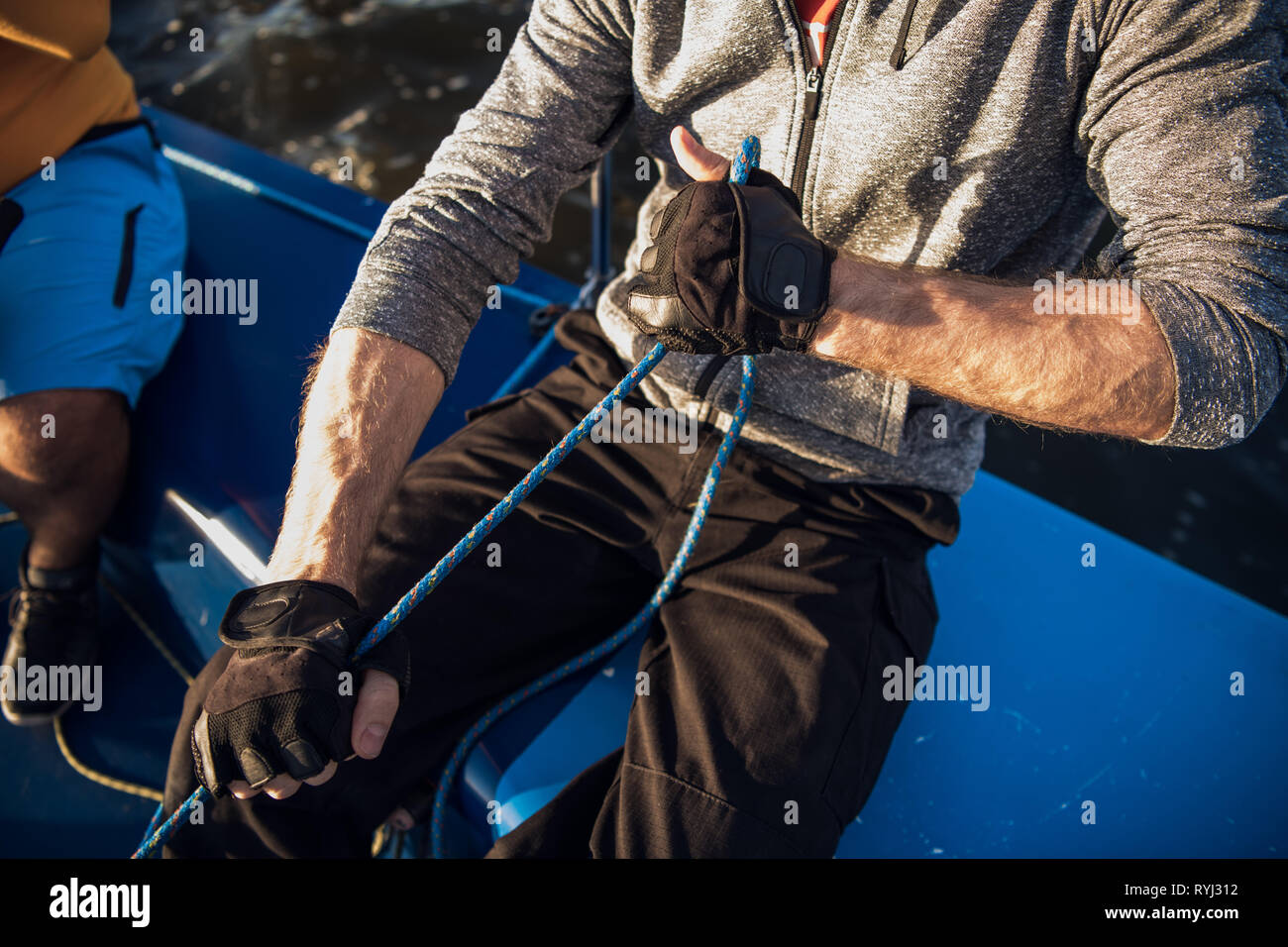 Close-up of male hands in gloves pulling rope of sailboat while mooring ...