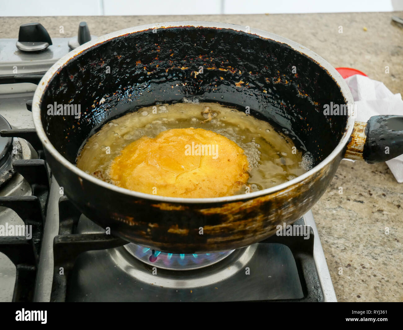 an arepa been fried in a pan in a gas stove covered by oil typical food ...