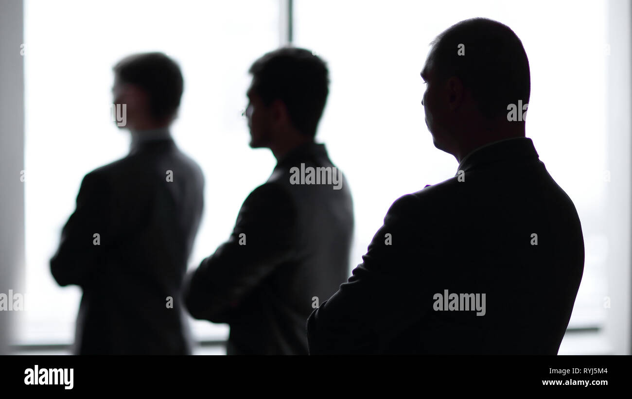 back view three employees as they look out on a large window ...