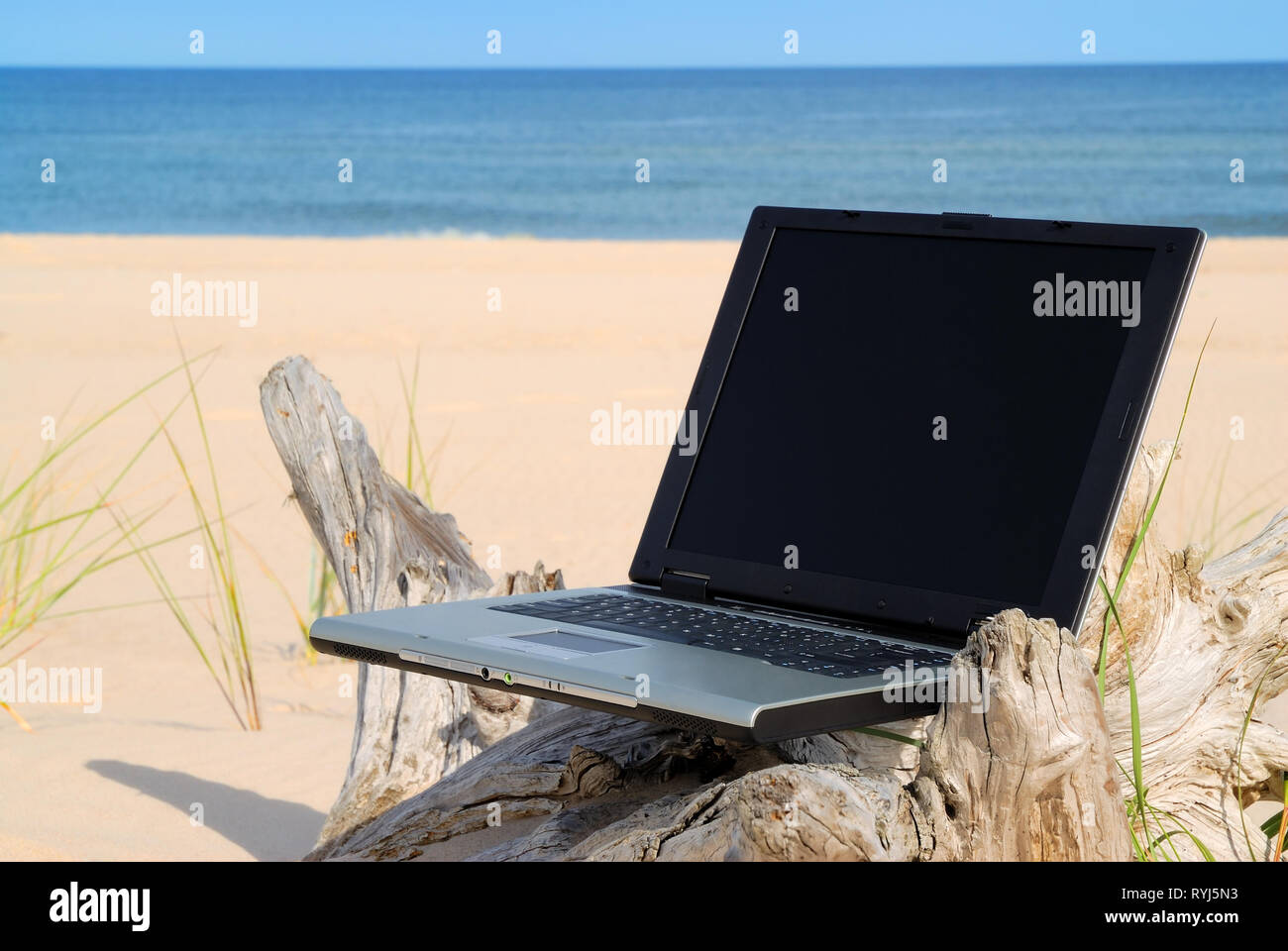 Modern laptop lying on sand. Beach and clean blue sky in background ...