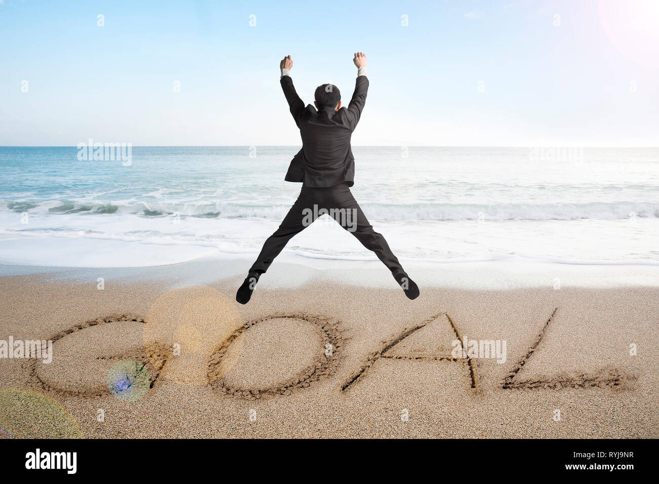 Jumping businessman cheering for goal word written on sand beach ...