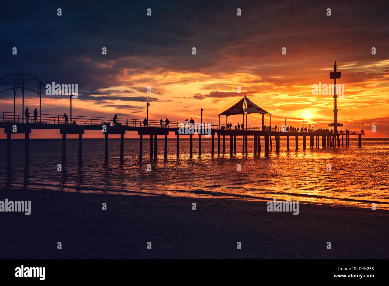 Iconic Brighton jetty with people silhouettes enjoying dramatic sunset ...