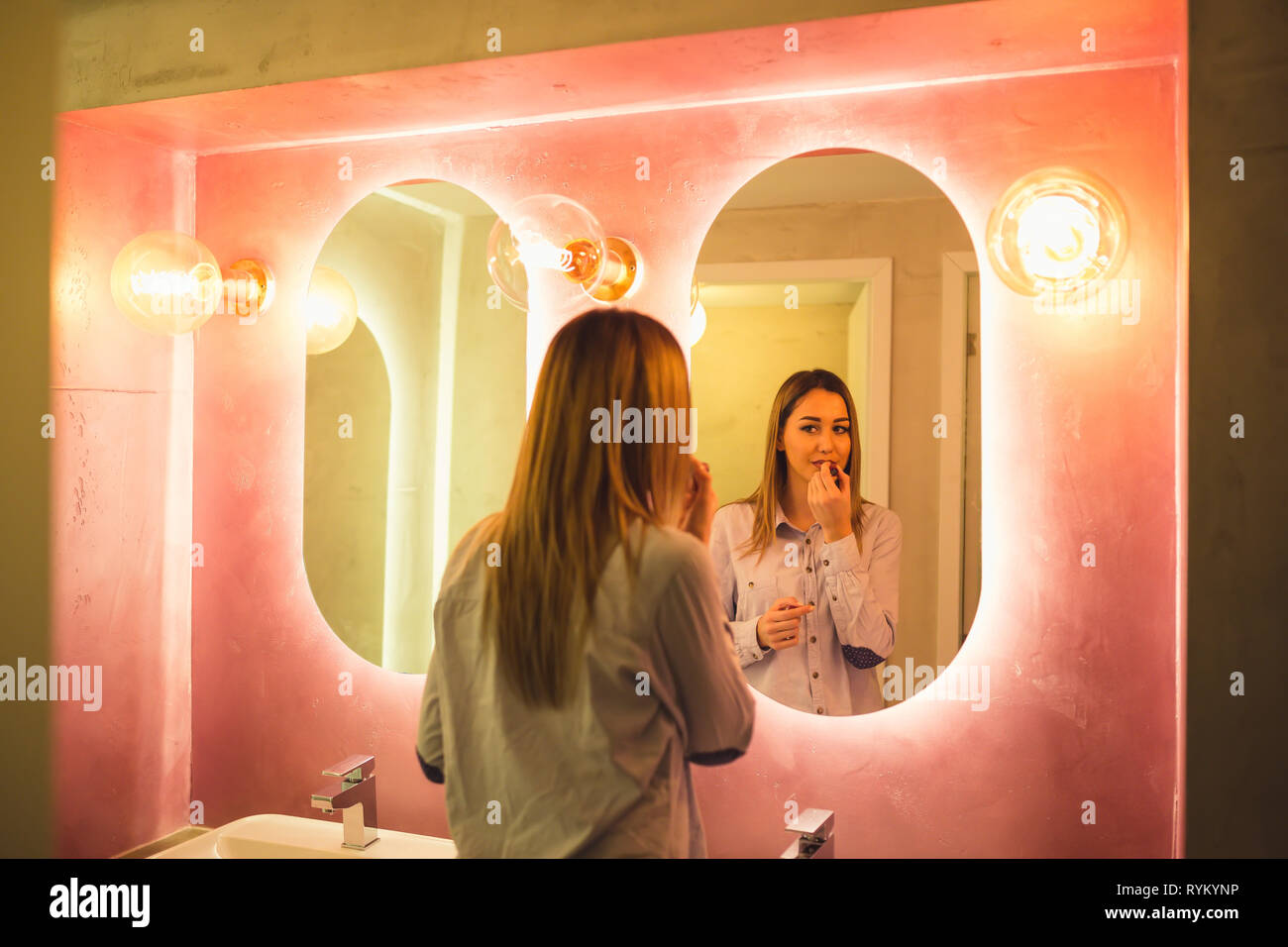 The woman paints lips in the toilet. Attractive happy woman applying ...