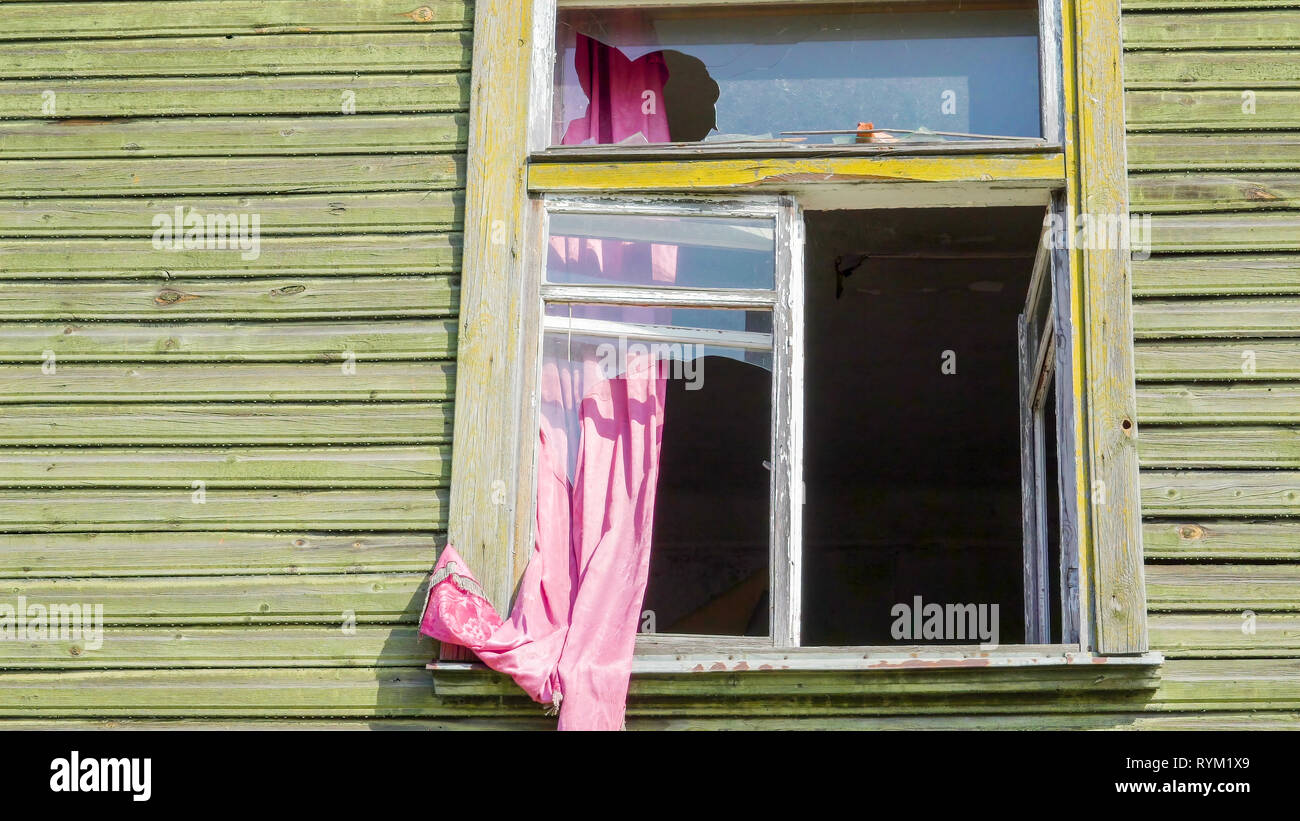 A broken glass of the window of the house with the pink curtain inside ...