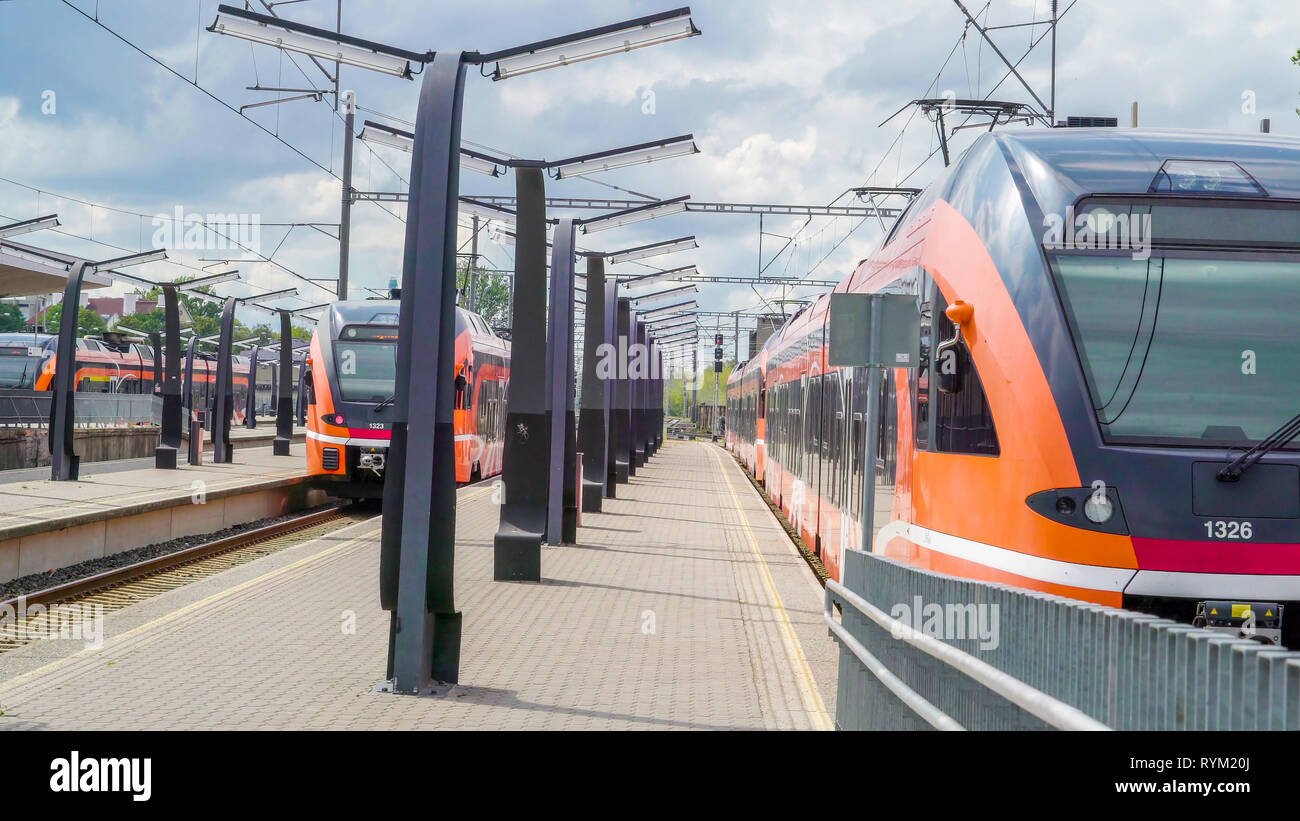 An orange modern train on the railway station boarding some passengers ...