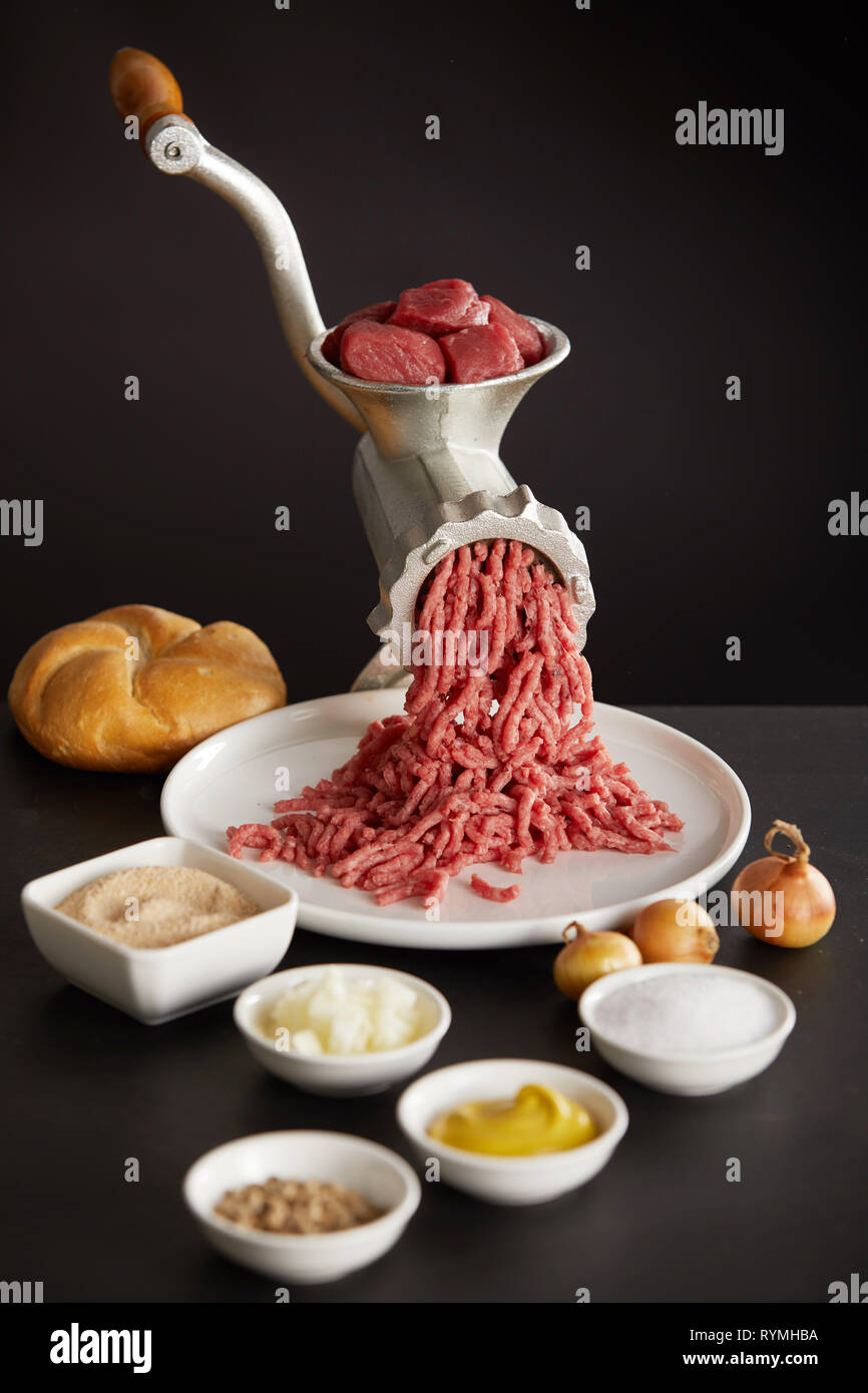 Grinder with minced meat and cooking ingredients in white bowls on ...