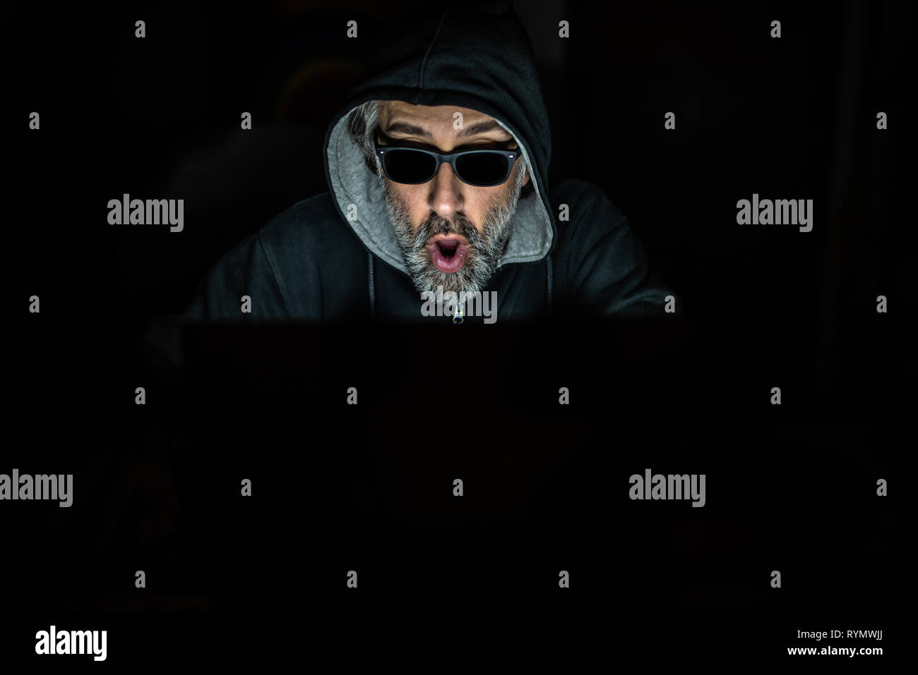 male hacker with beard and sunglasses working on his laptop, amazed and ...
