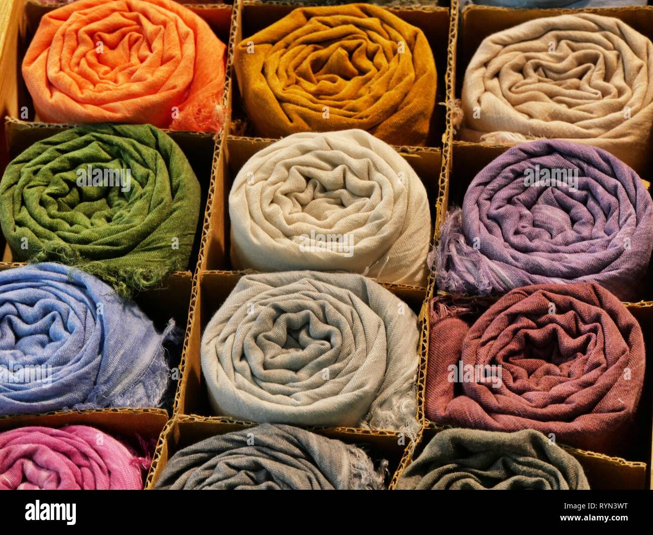 Variety of rolled silk scarves of different vivid colours arranged in a ...
